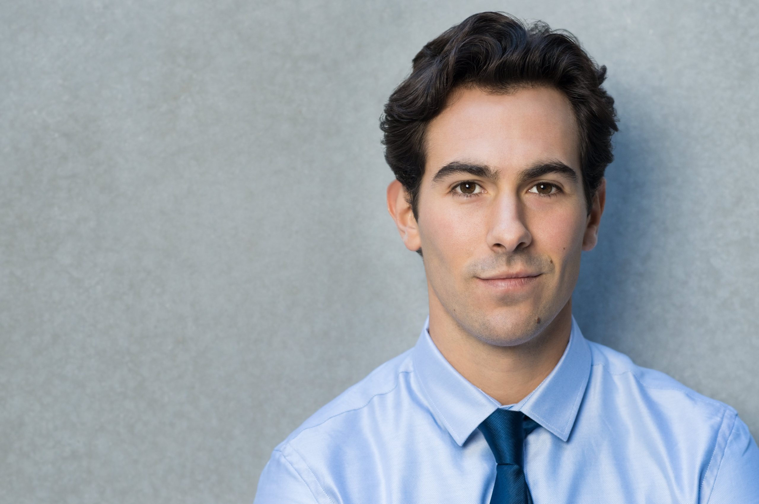 Happy young businessman leaning against grey wall. Portrait of a ...
